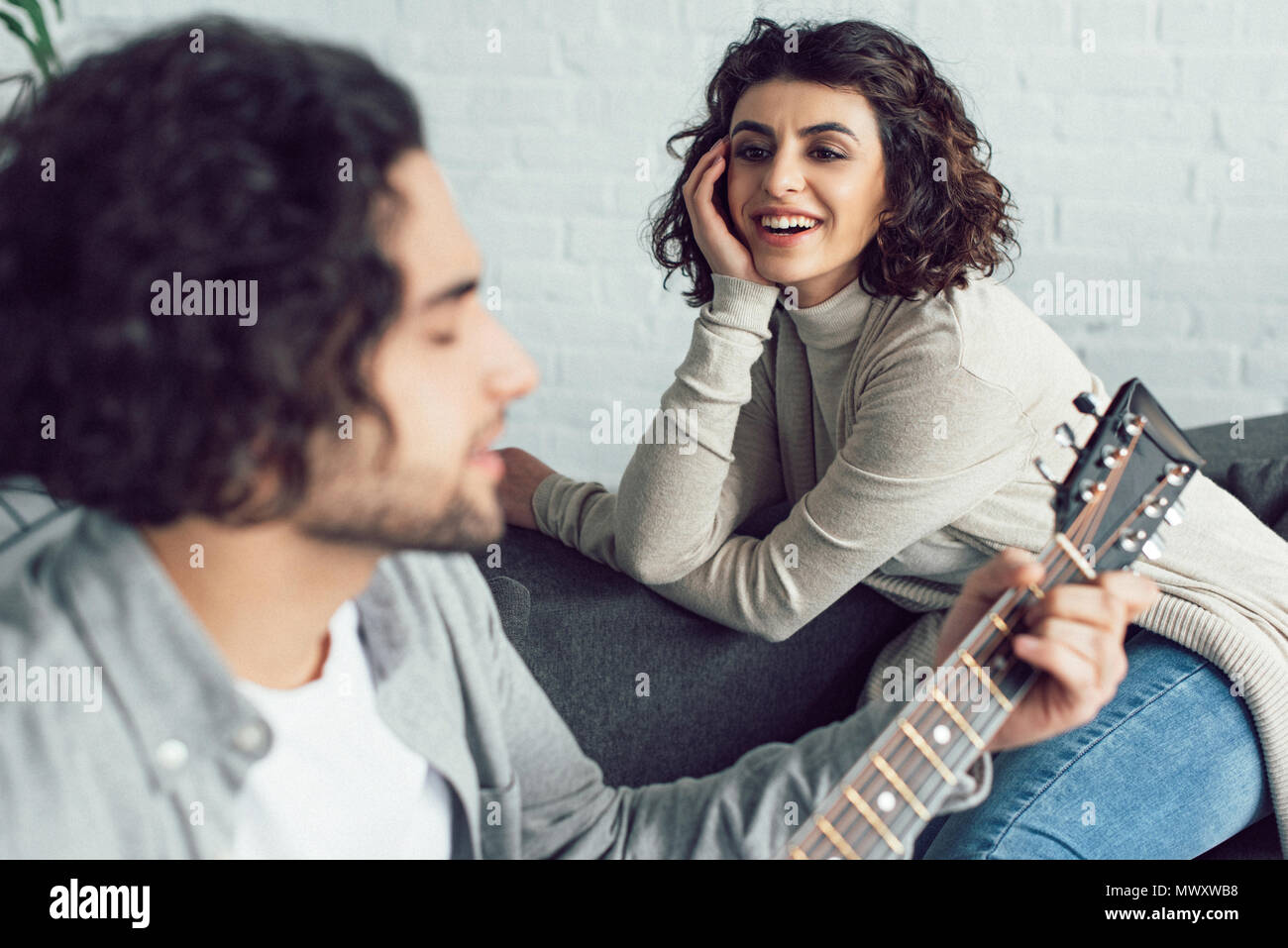 boyfriend playing guitar and singing for smiling girlfriend at home ...