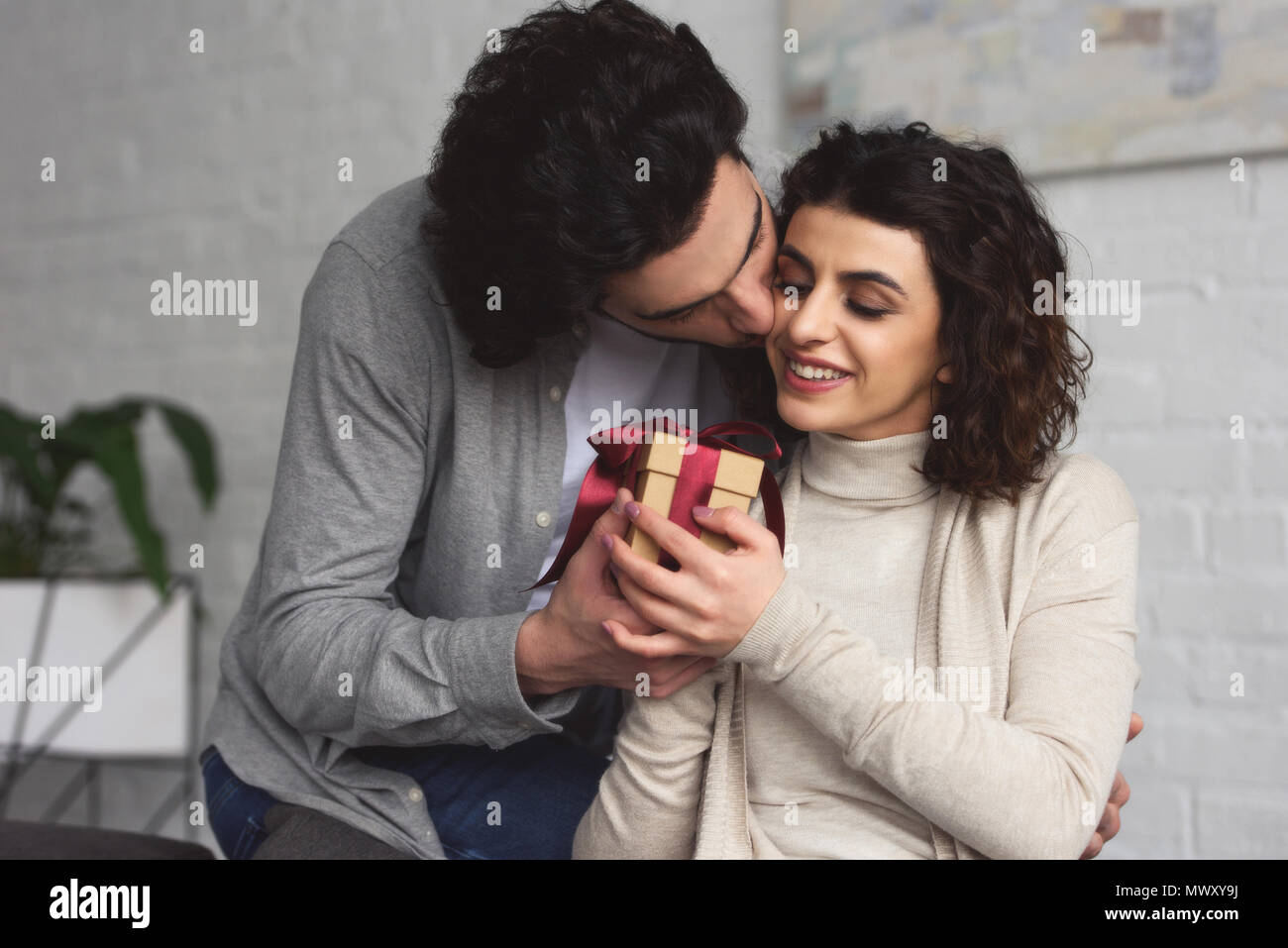 boyfriend presenting gift to girlfriend and kissing her at home Stock ...