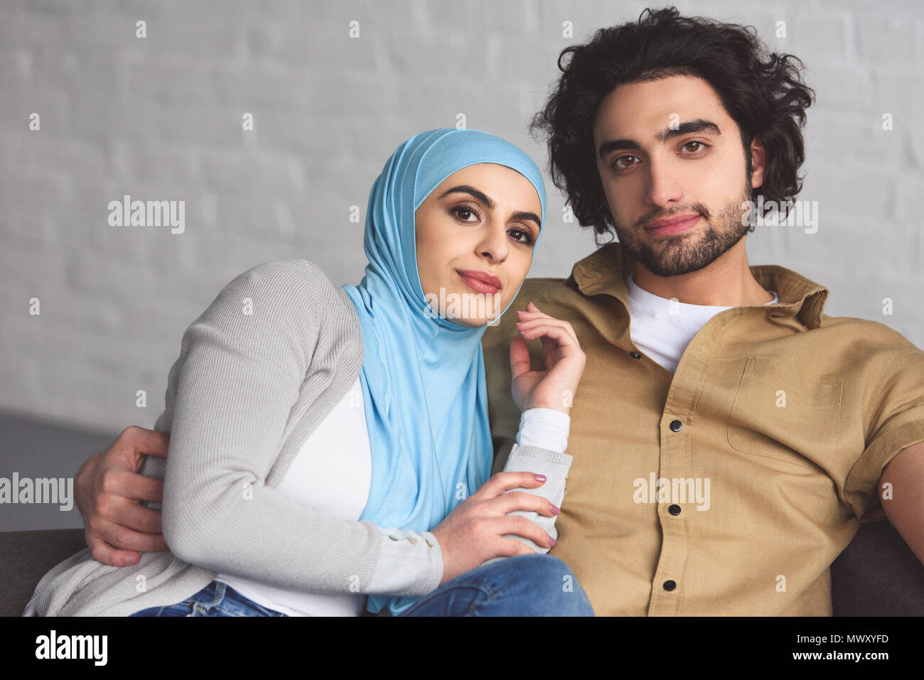 happy muslim couple sitting on sofa in living room and looking at ...
