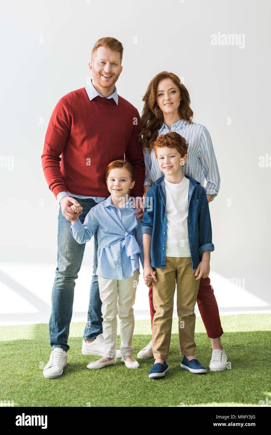 happy redhead family standing together and smiling at camera on grey ...