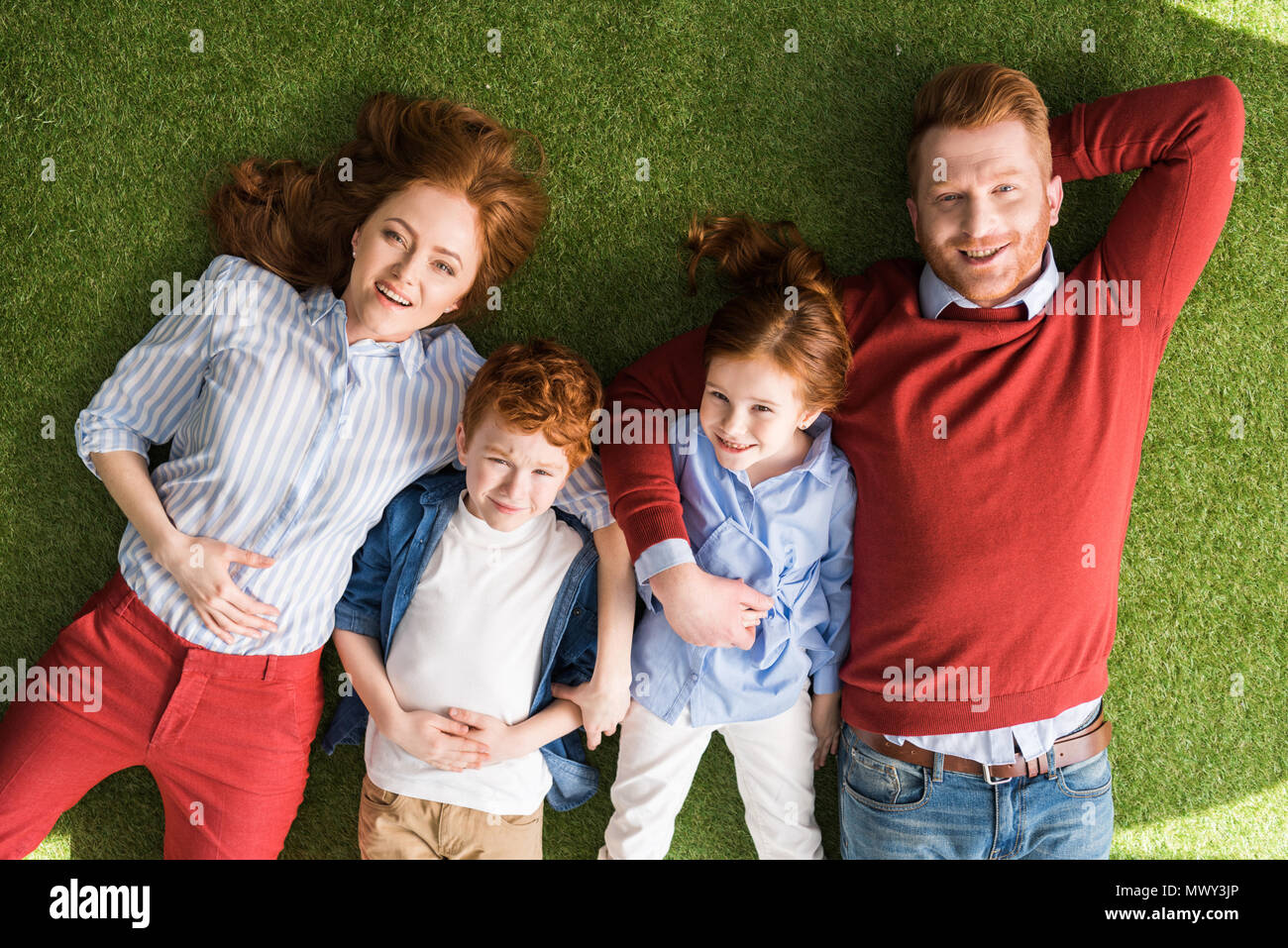 top view of happy redhead family with two kids lying together on grass ...
