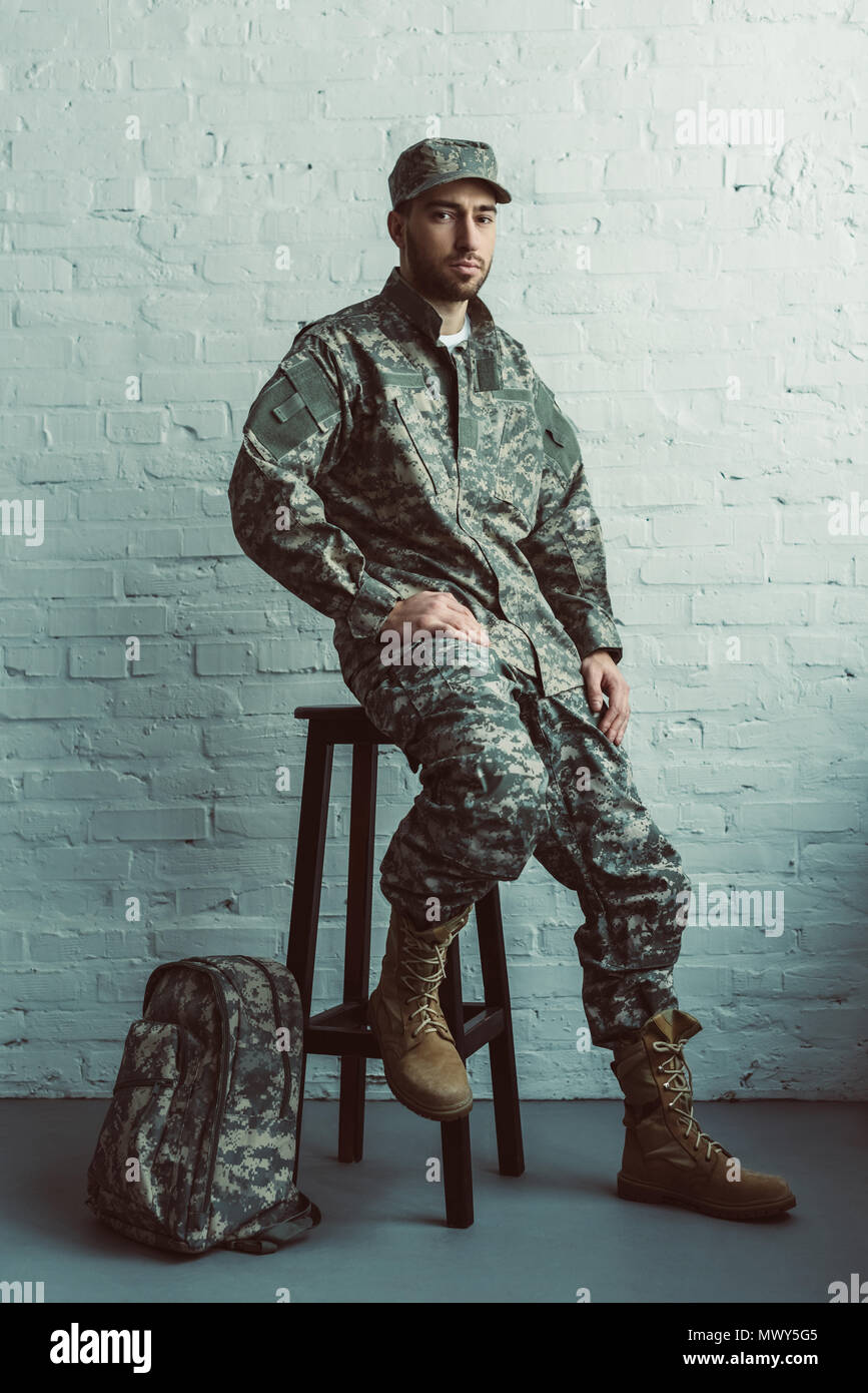 soldier in military uniform sitting on chair against white brick wall ...