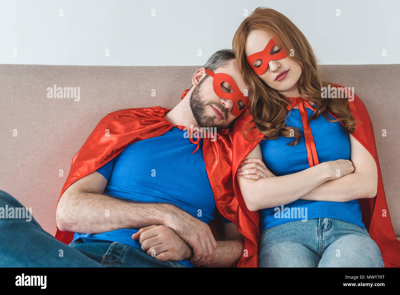 tired couple of superheroes in masks and cloaks sleeping together on ...