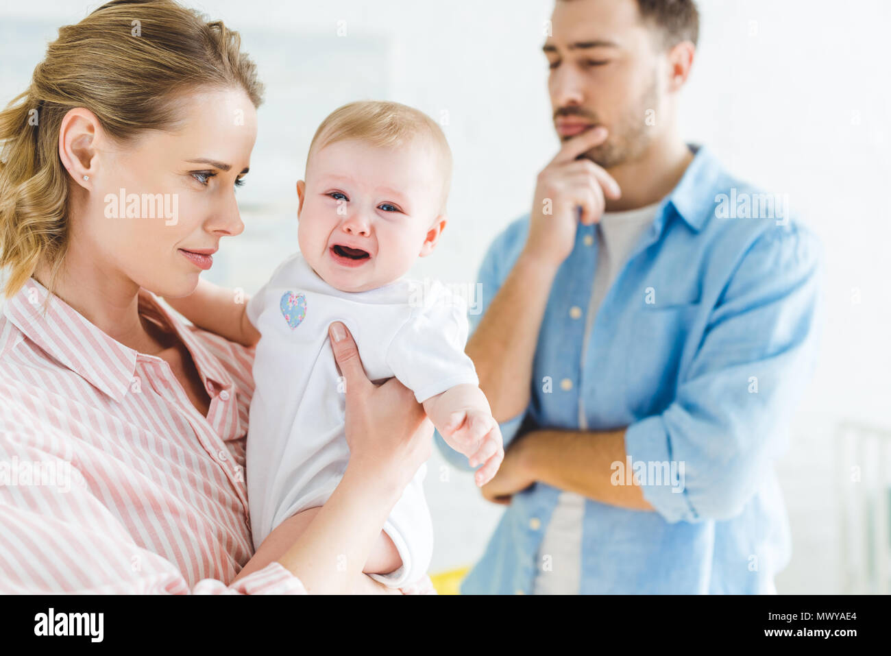 Mother holding crying infant daughter on hands and thoughtful father ...