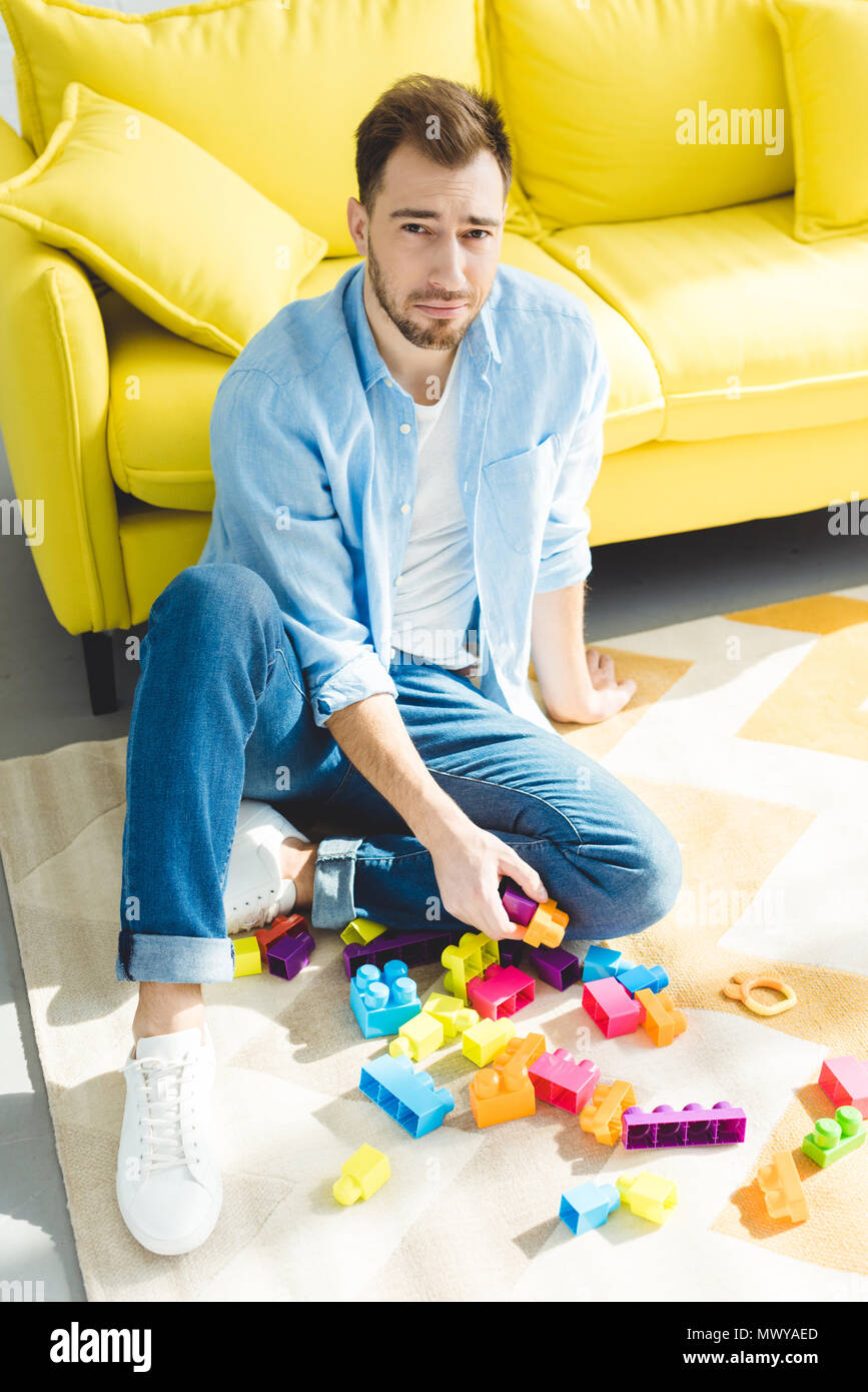 Stylish young man sitting on rug with plastic blocks Stock Photo - Alamy