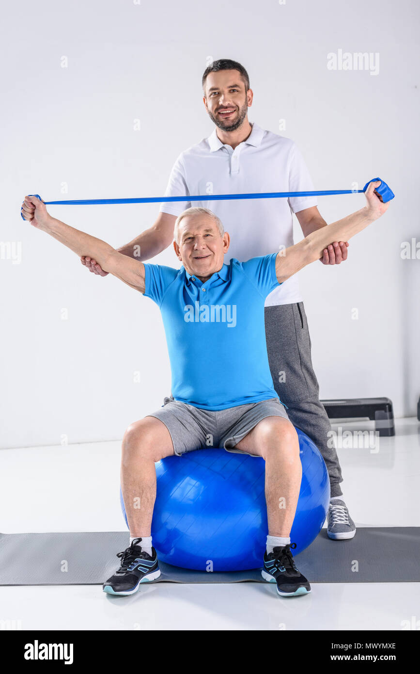 rehabilitation therapist assisting smiling senior man exercising with ...