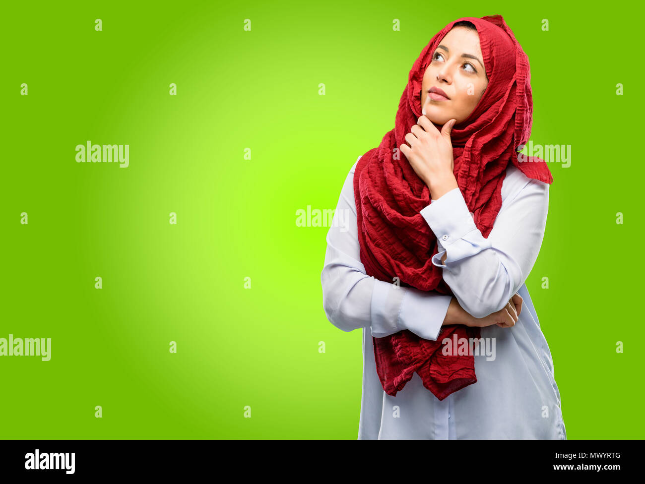 Young arab woman wearing hijab thinking and looking up expressing doubt ...