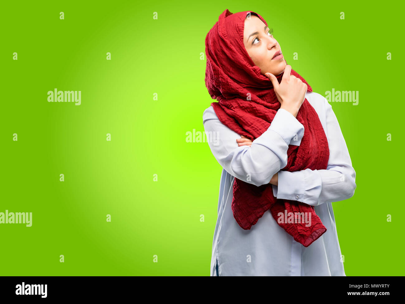 Young arab woman wearing hijab thinking and looking up expressing doubt ...