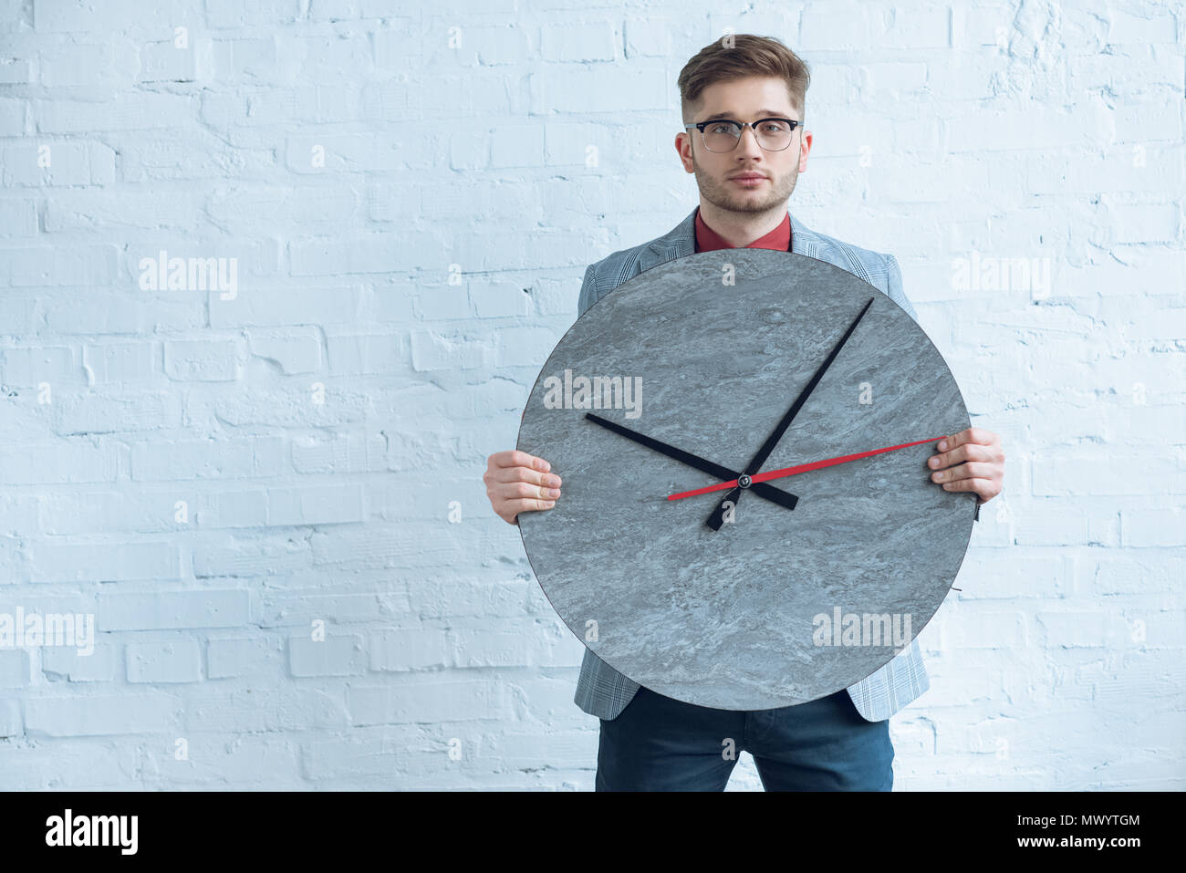 Man holding large clock in front of him by white wall Stock Photo - Alamy