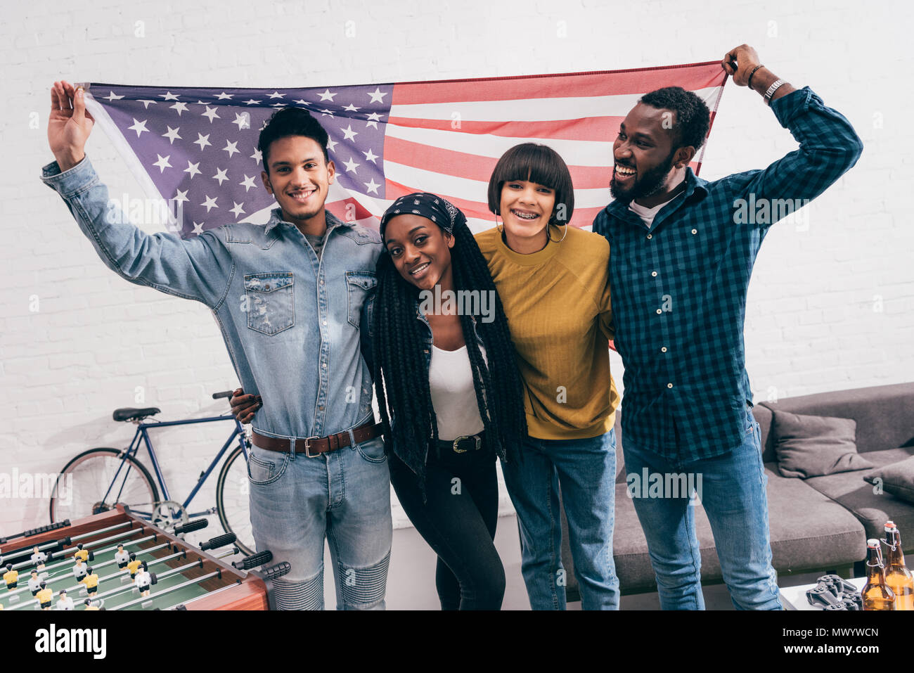 young multiethnic friends with flag of USA standing near table football ...