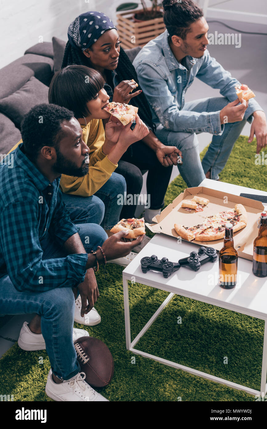 high angle view of multiethnic friends eating pizza and watching ...
