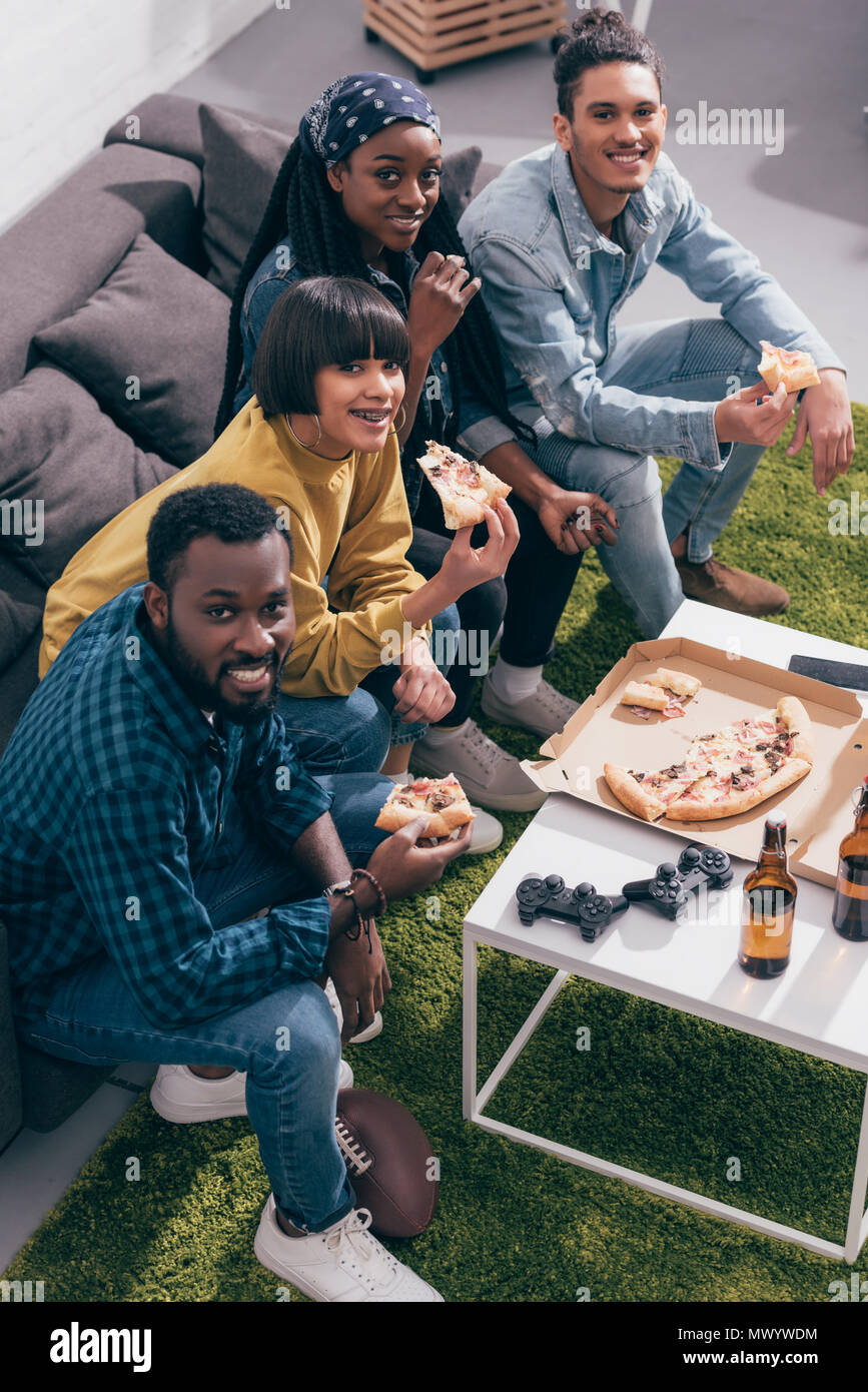 high angle view of young multiethnic friends sitting with pizza sitting ...