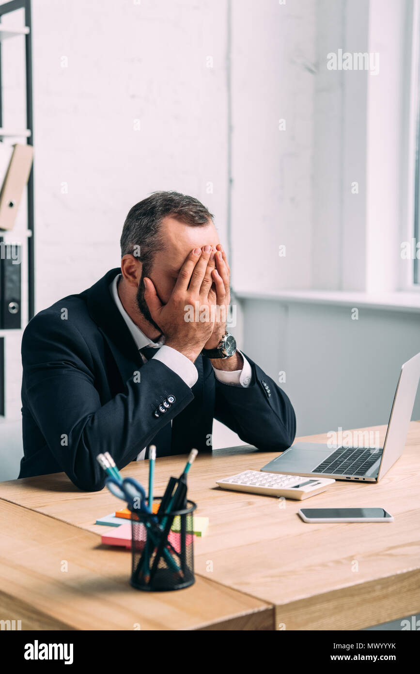 obscured view of overworked businessman covering face with hands at ...