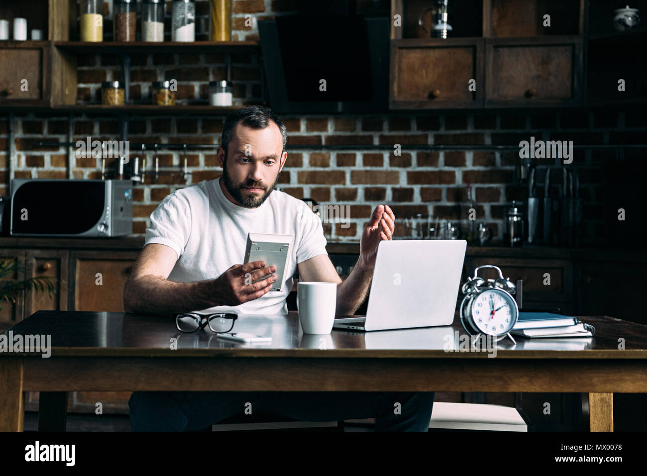 shocked young man looking at calculator after counting bills to pay ...
