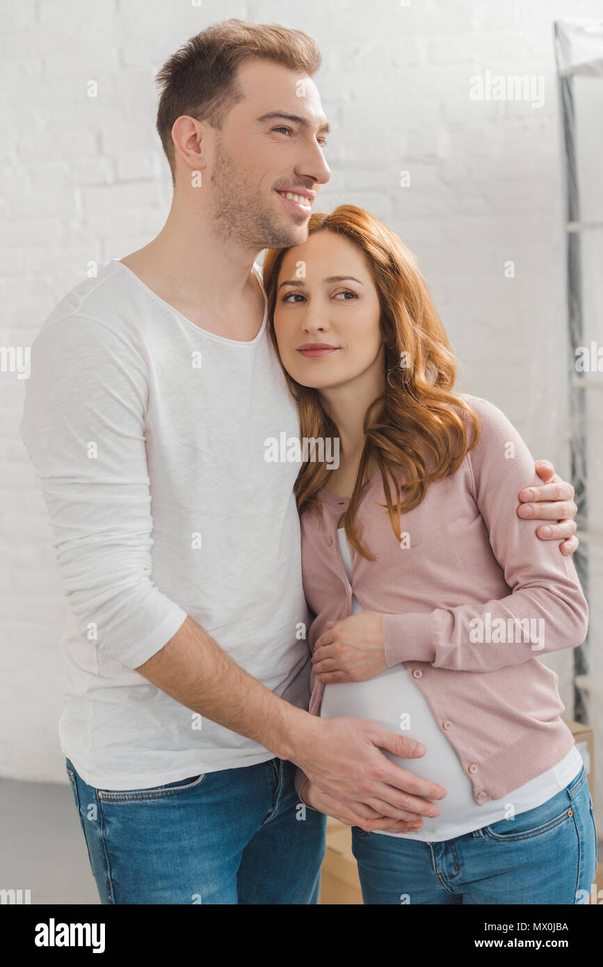 happy pregnant couple embracing and looking away at home Stock Photo ...