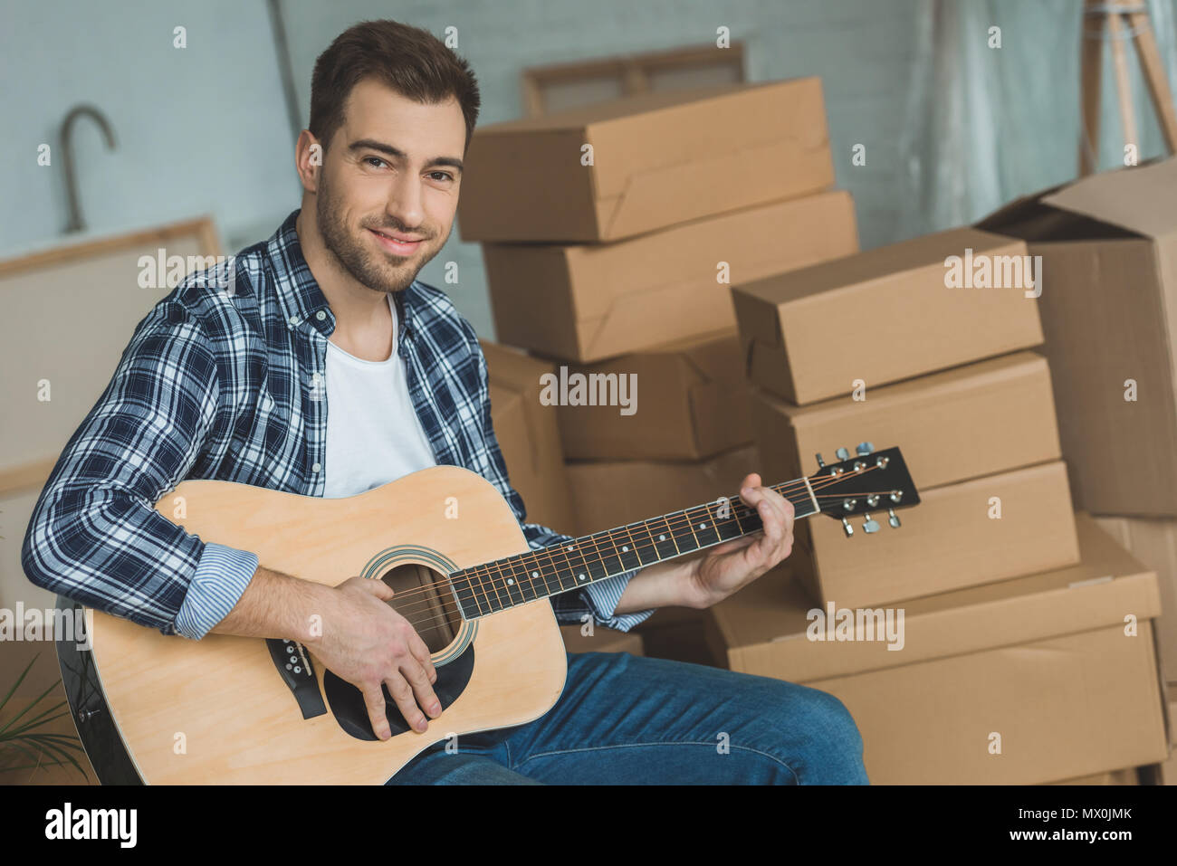 Portrait Of Smiling Man With Acoustic Guitar At New Home With Cardboard