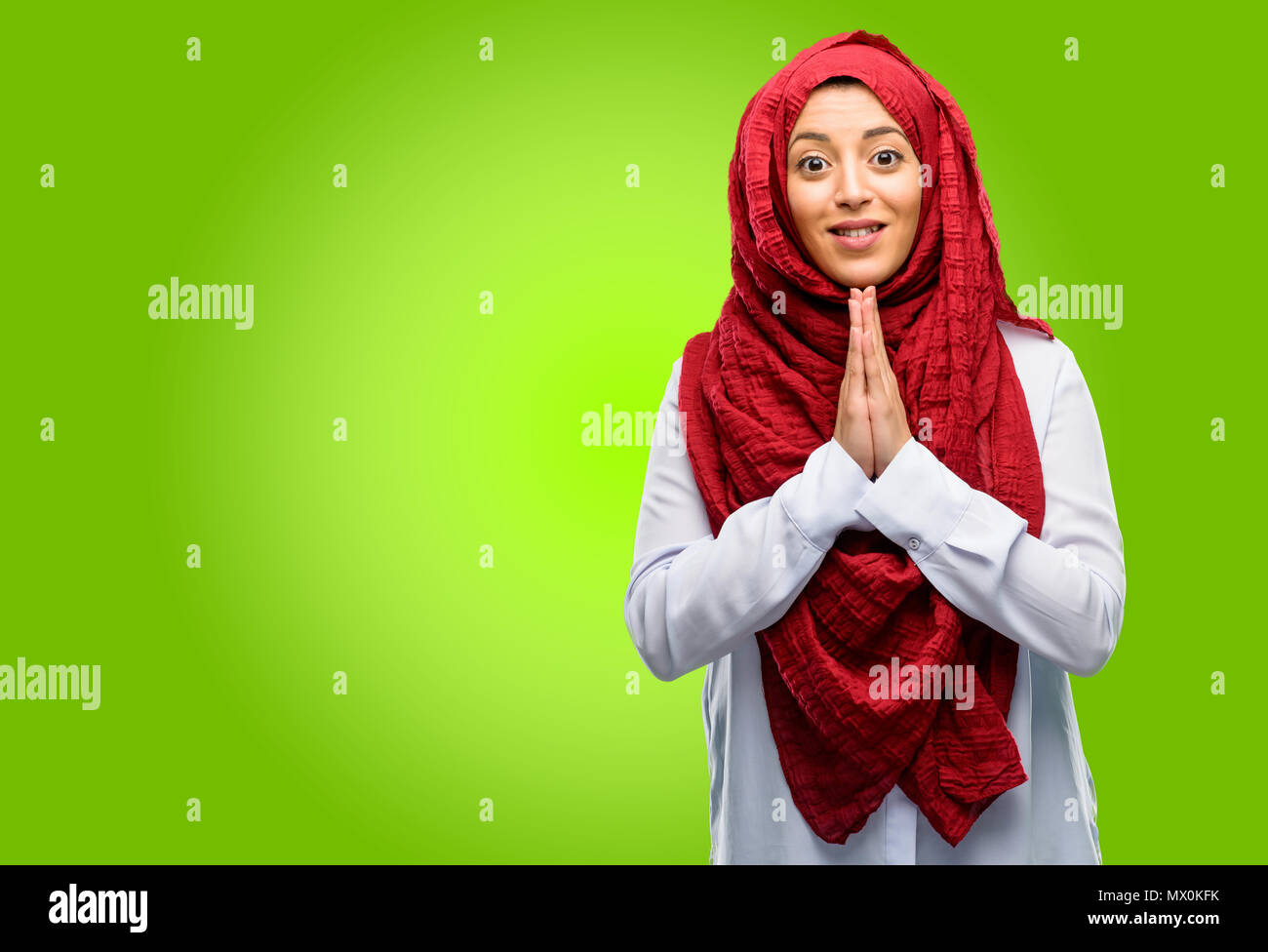 Young arab woman wearing hijab with hands together in praying gesture ...