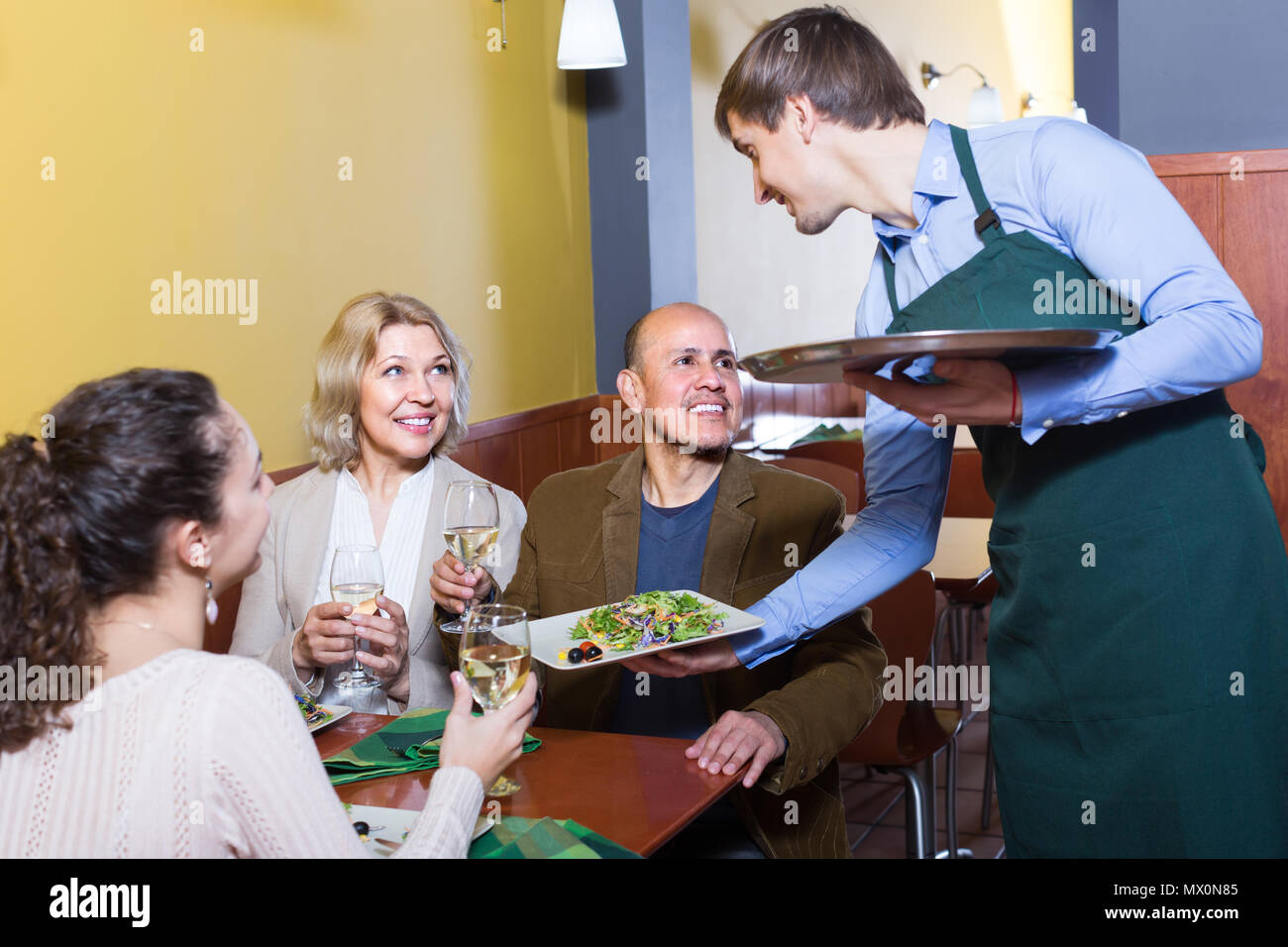 Friendly young waiter serving table with happy adults in restaurant ...