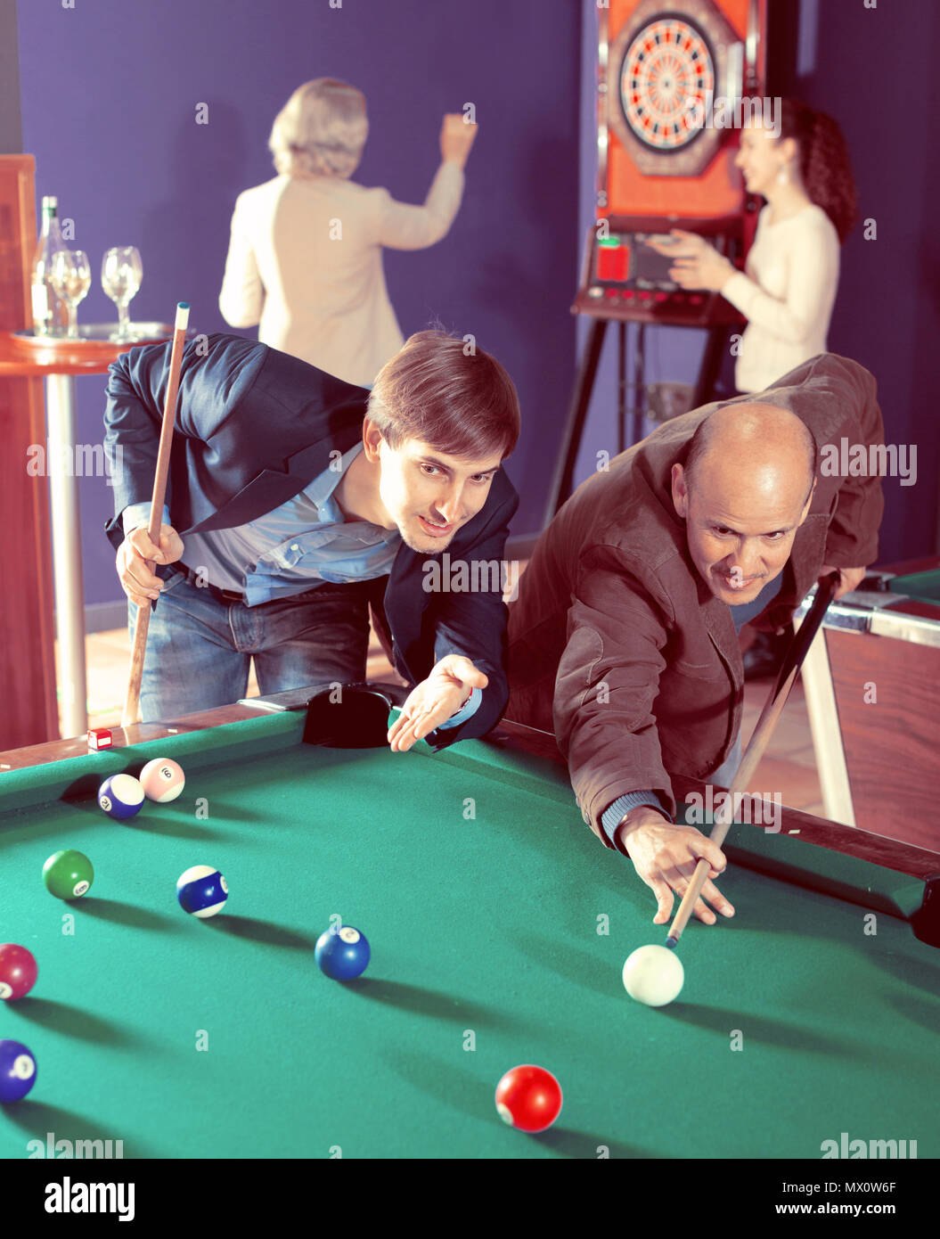 Happy group of friends of different ages playing billiards and smiling ...