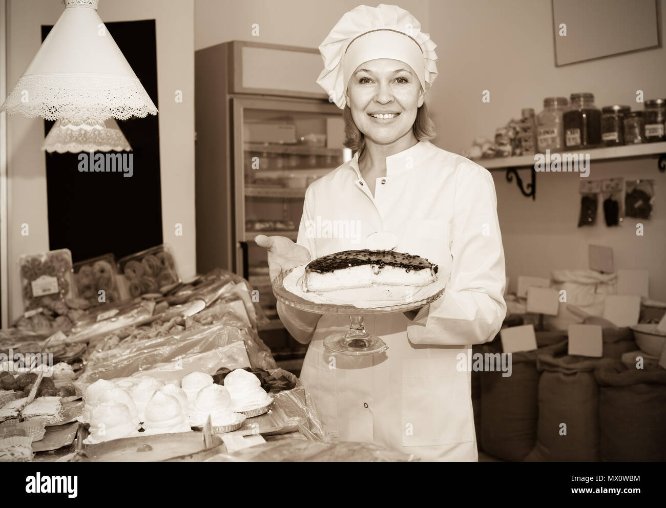 Portrait of positive mature female baker smiling in bakery Stock Photo ...