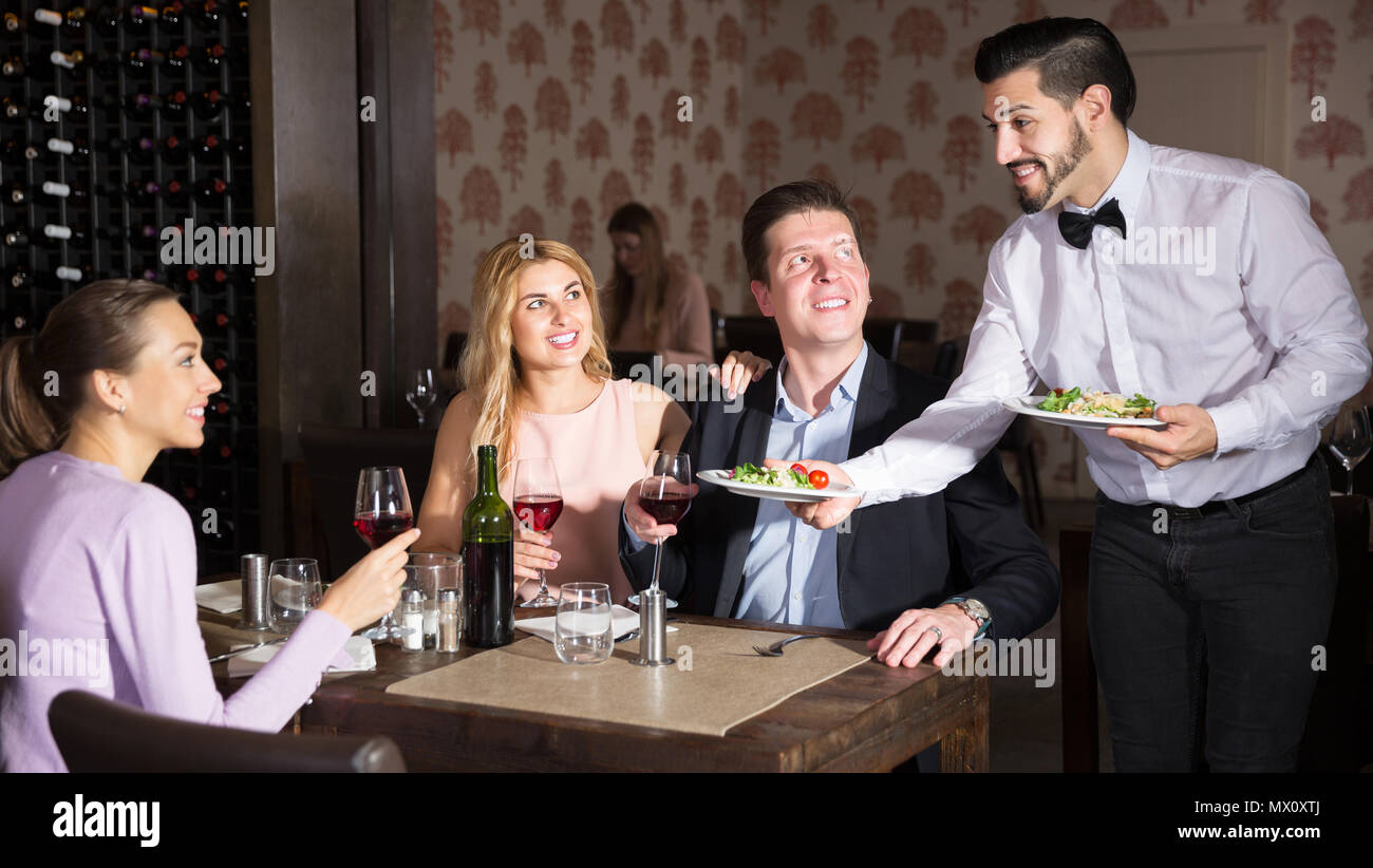 Polite smiling waiter bringing ordered dishes to guests at restaurant ...