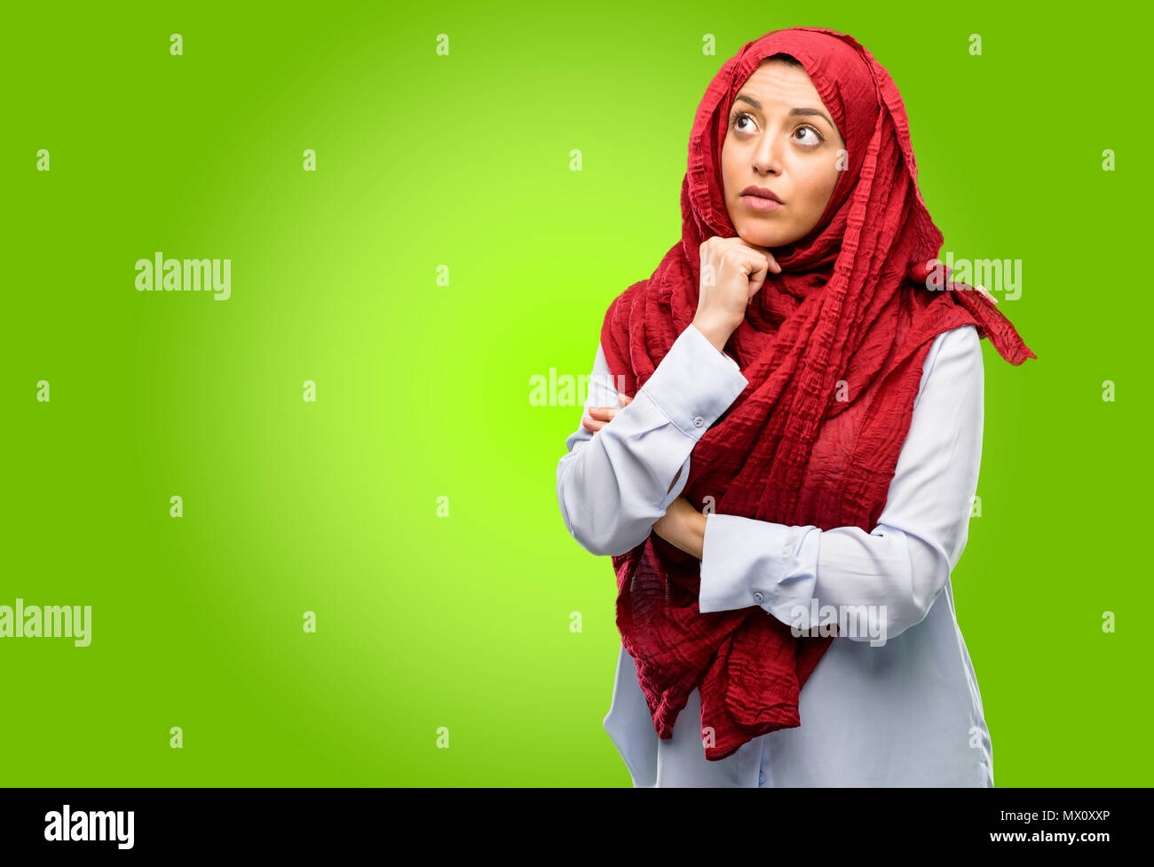 Young arab woman wearing hijab thinking and looking up expressing doubt ...