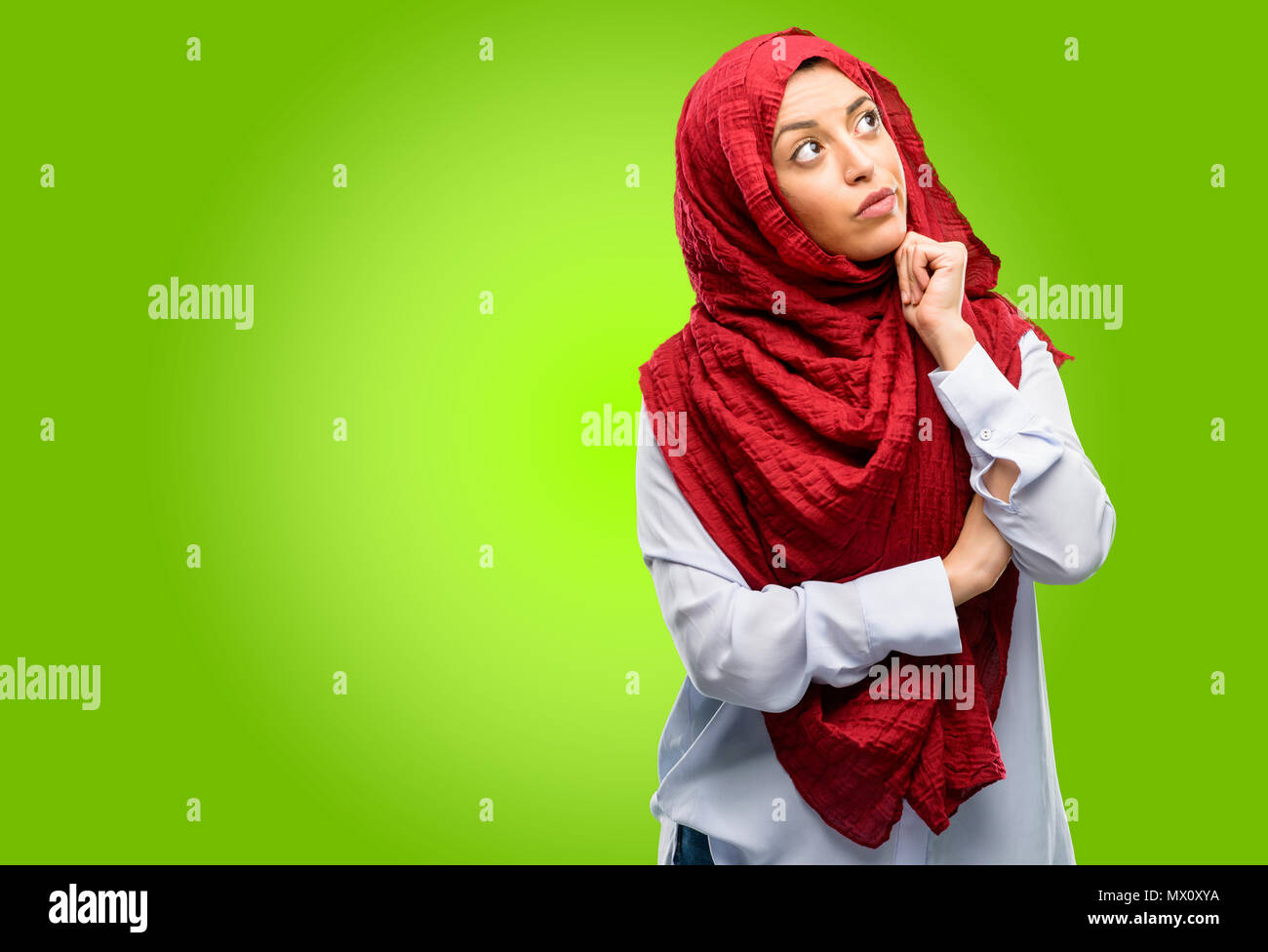 Young arab woman wearing hijab thinking and looking up expressing doubt ...