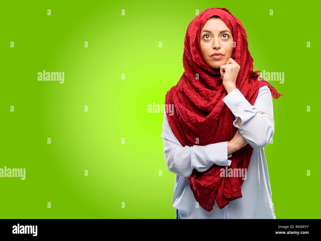 Young arab woman wearing hijab thinking and looking up expressing doubt ...