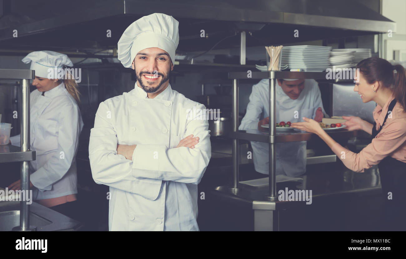 Portrait of satisfied cheerful positive chef on restaurant kitchen with ...