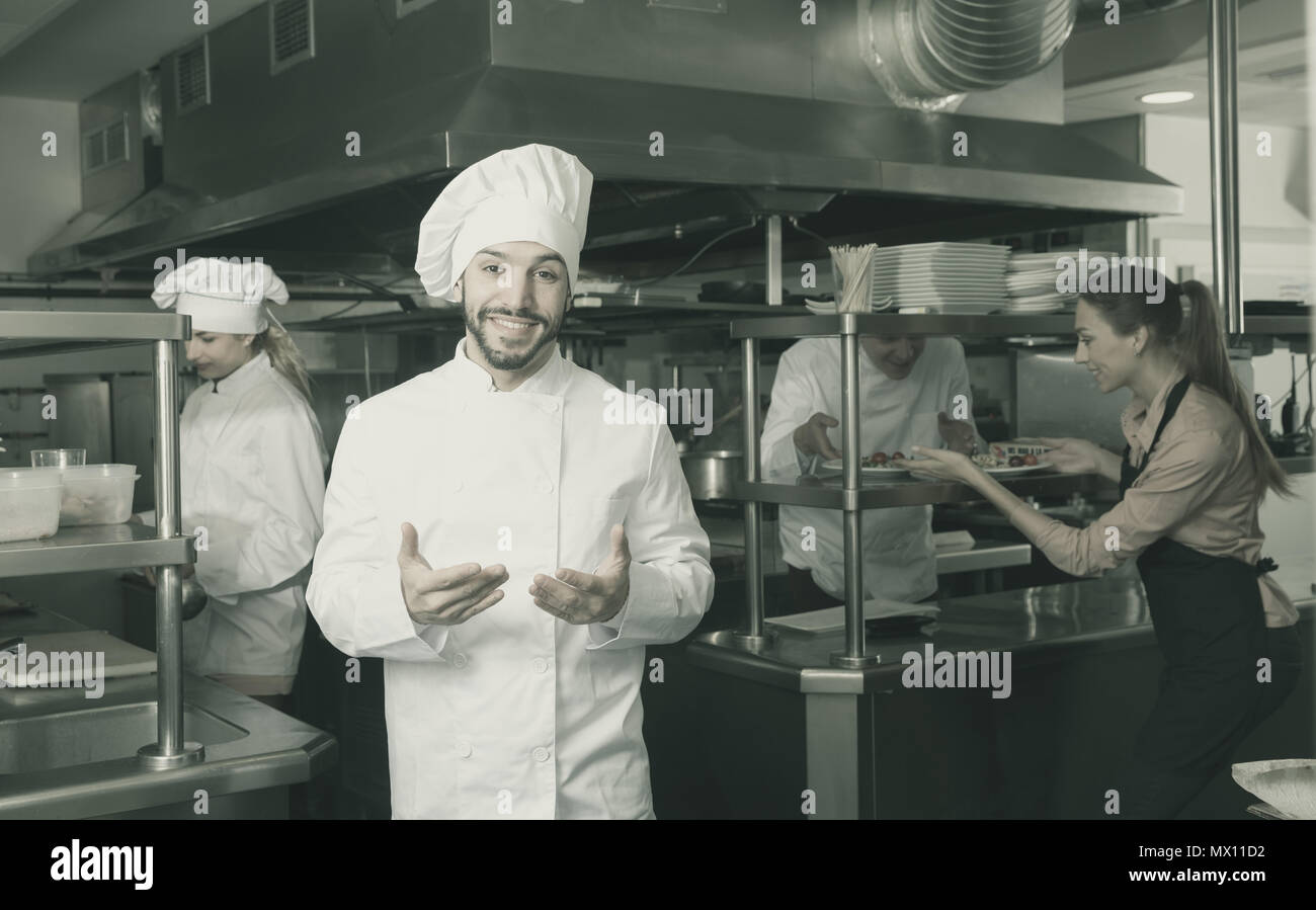 Portrait of satisfied smiling chef on restaurant kitchen with busy ...