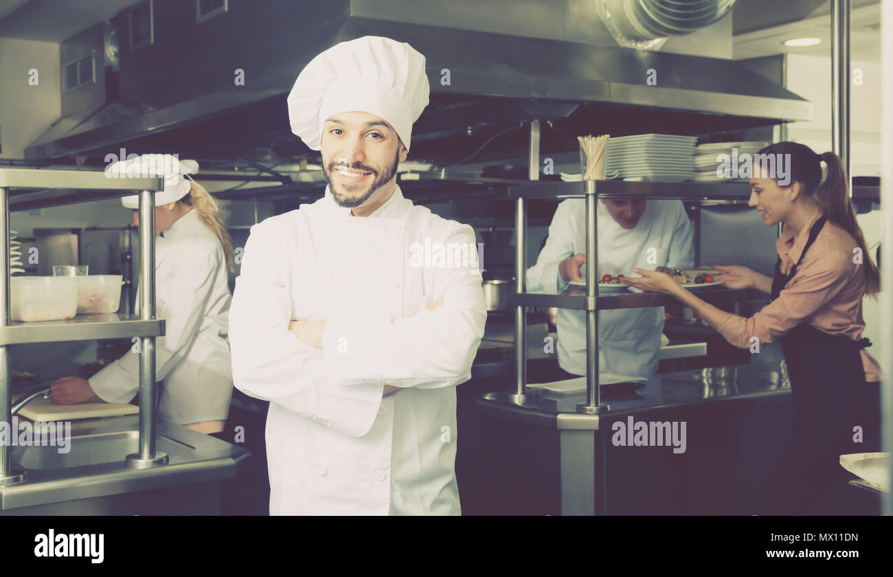 Positive chef of restaurant posing in kitchen on background with ...