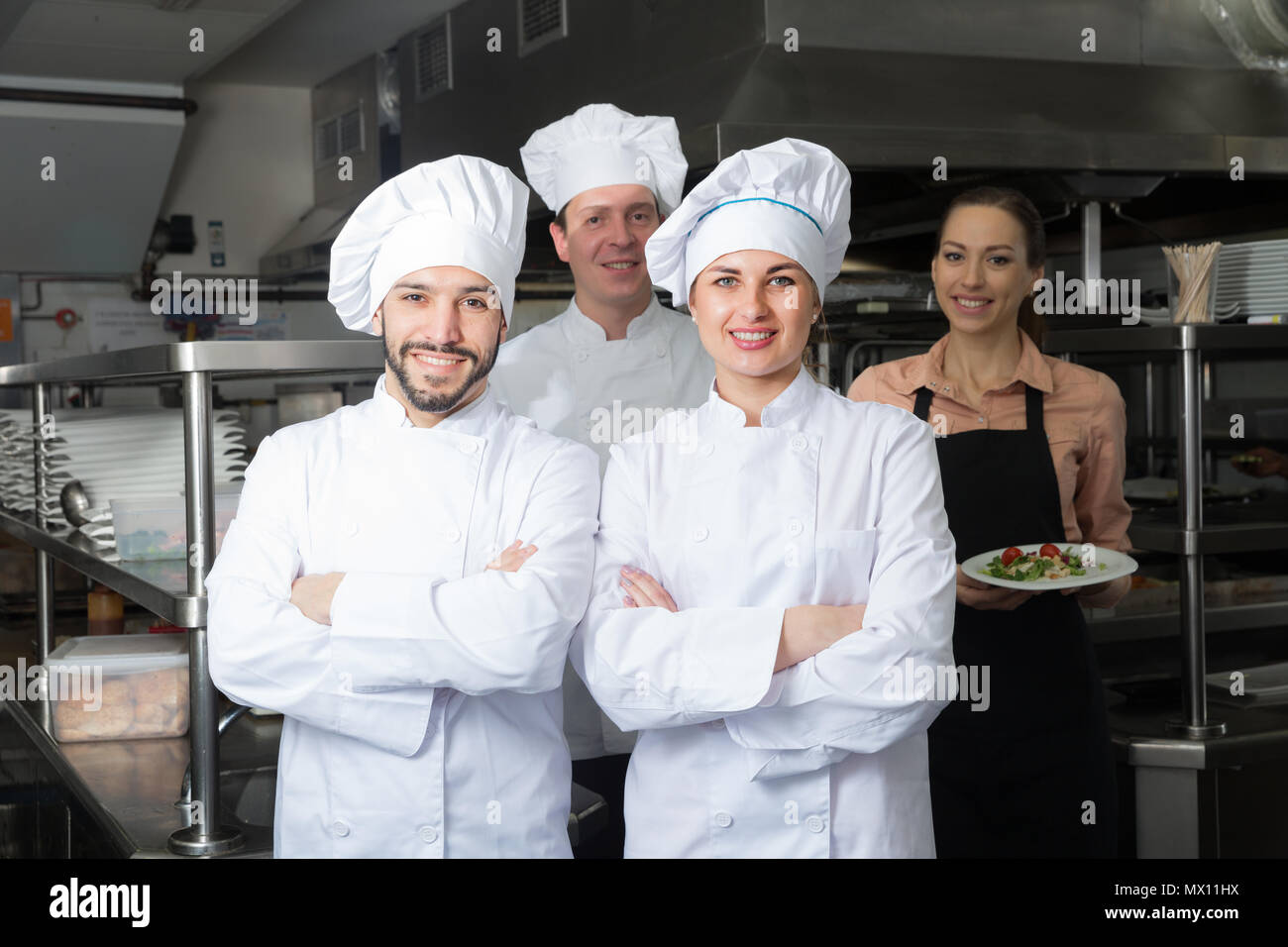 Portrait of two confident cheerful chefs in kitchen with staff of ...