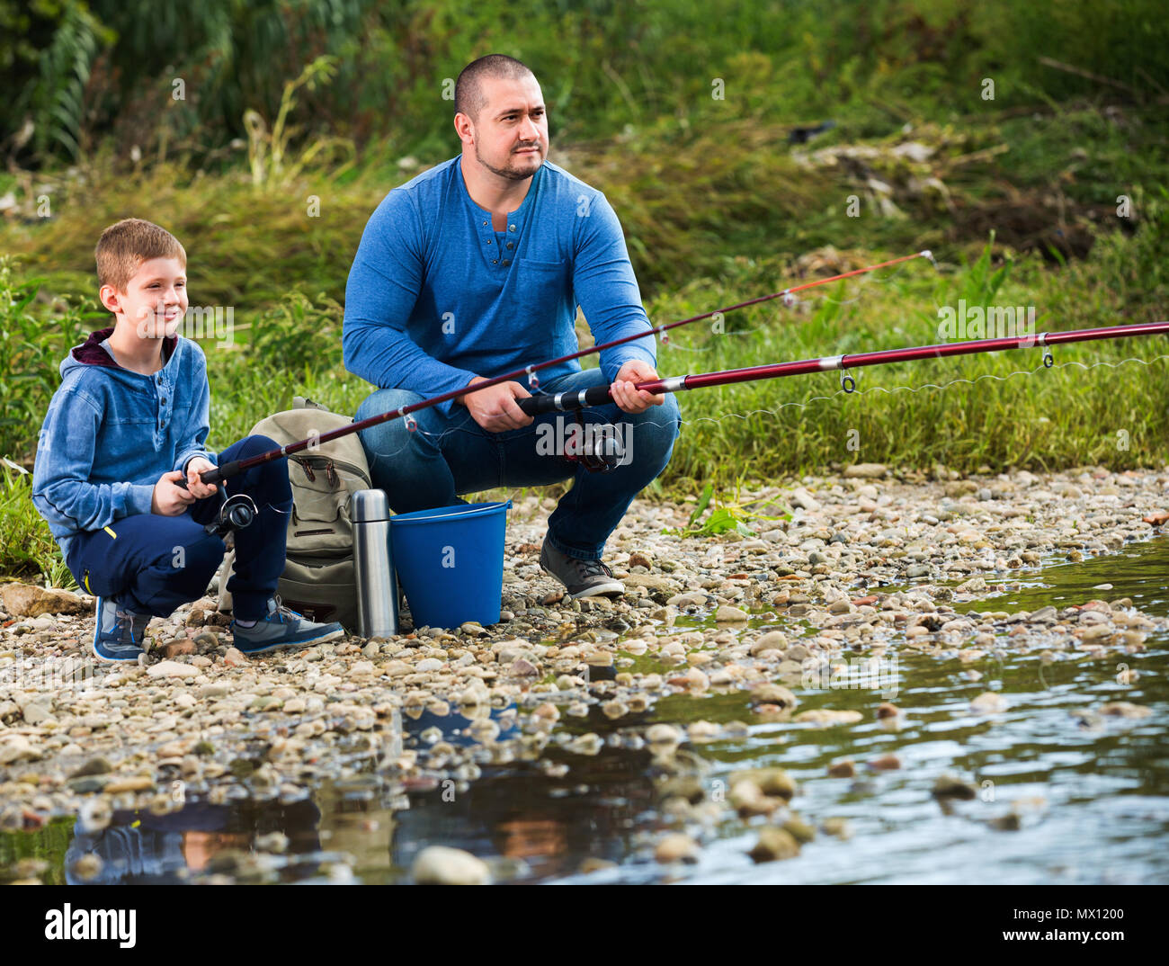 Portrait of positive father and smiling son fishing with rods in summer ...