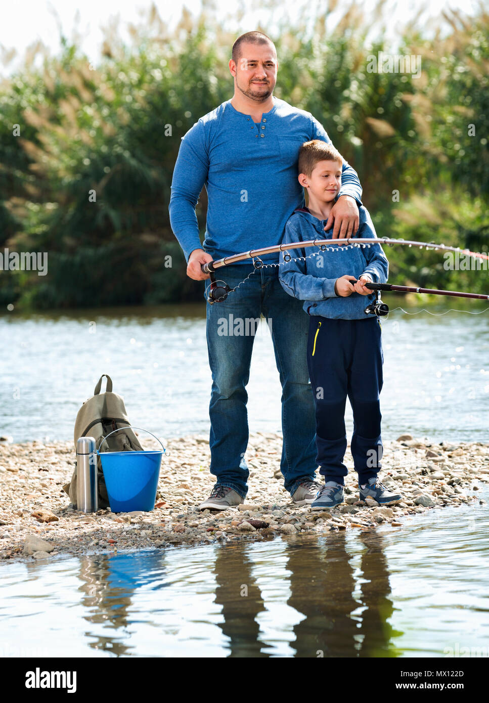 Portrait of glad father and cute son fishing with rods in summer day ...