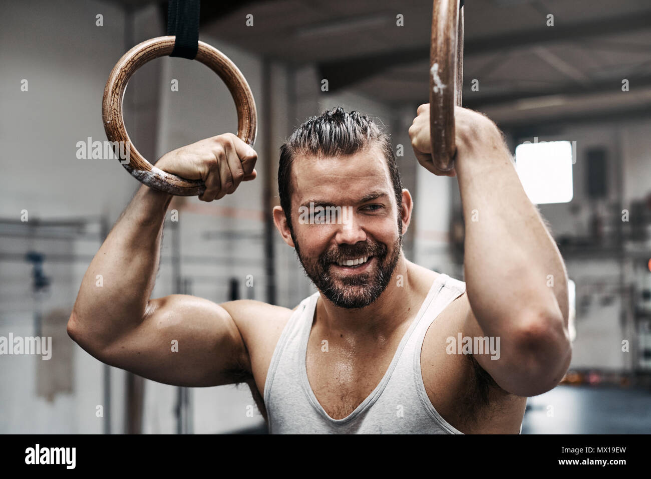 Fit young man in sportswear smiling while exercising on rings during a ...
