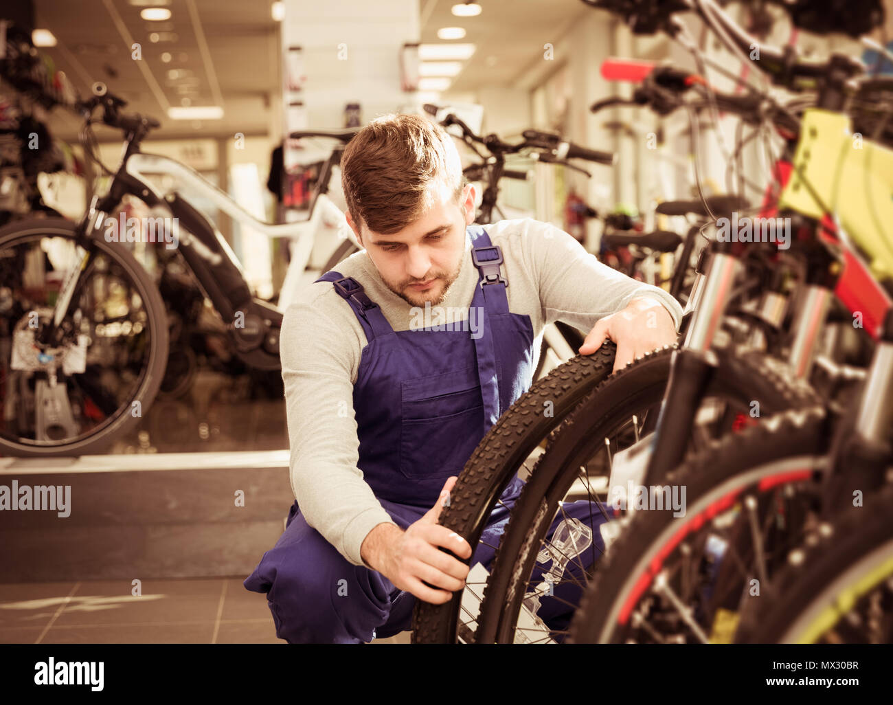 Portrait of young professional man checking tire on wheel in bicycle ...