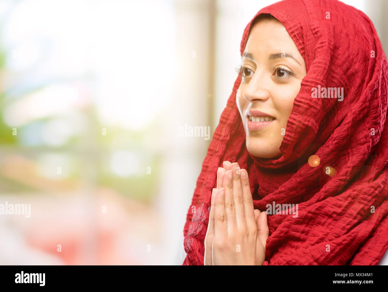 Young arab woman wearing hijab with hands together in praying gesture ...