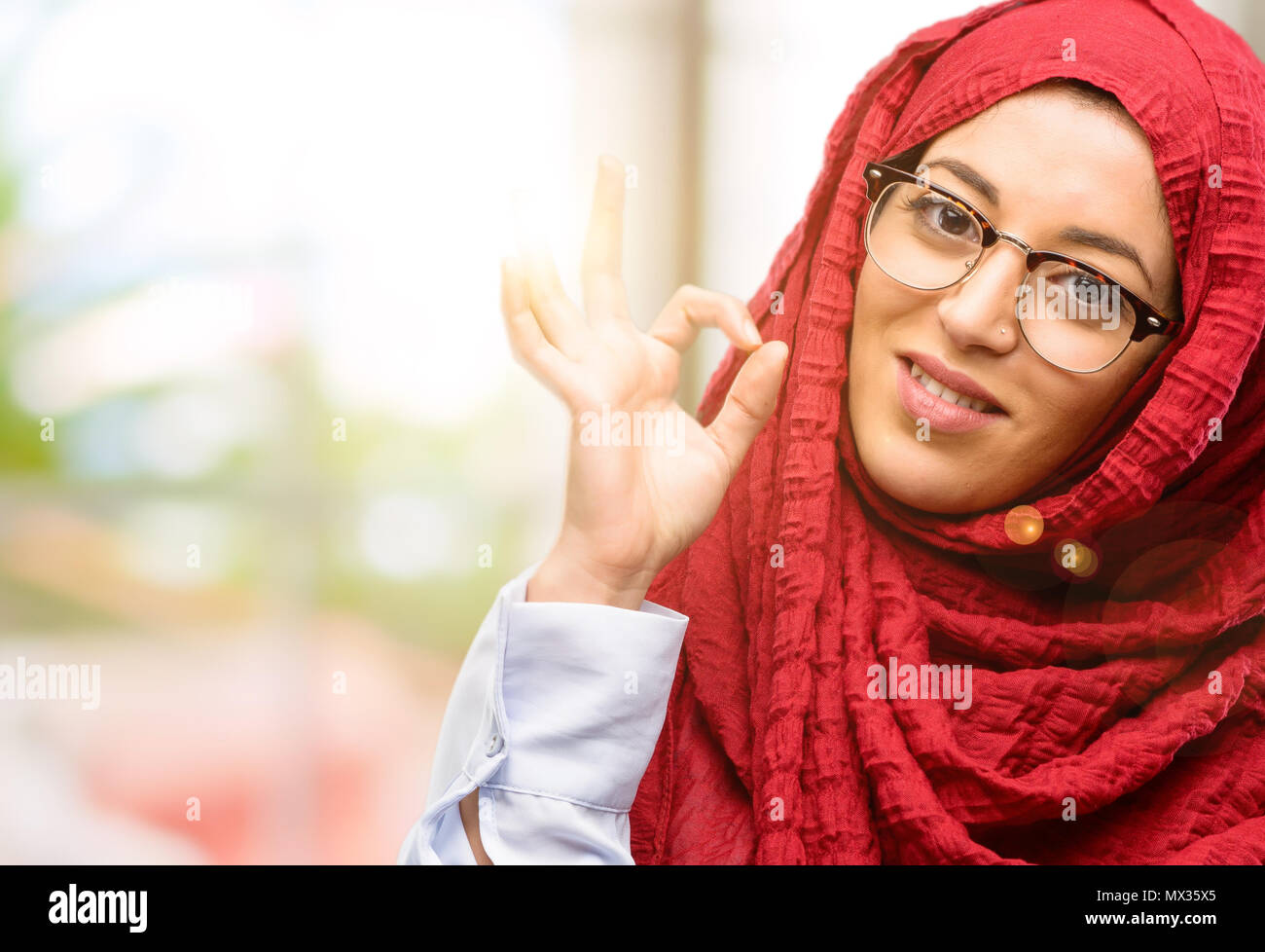 Young arab woman wearing hijab doing ok sign with hand, approve gesture ...