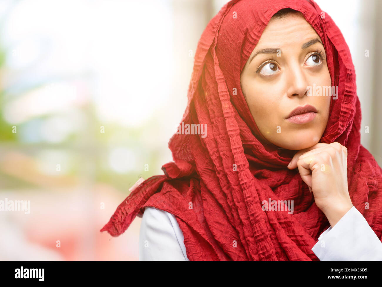 Young arab woman wearing hijab thinking and looking up expressing doubt ...