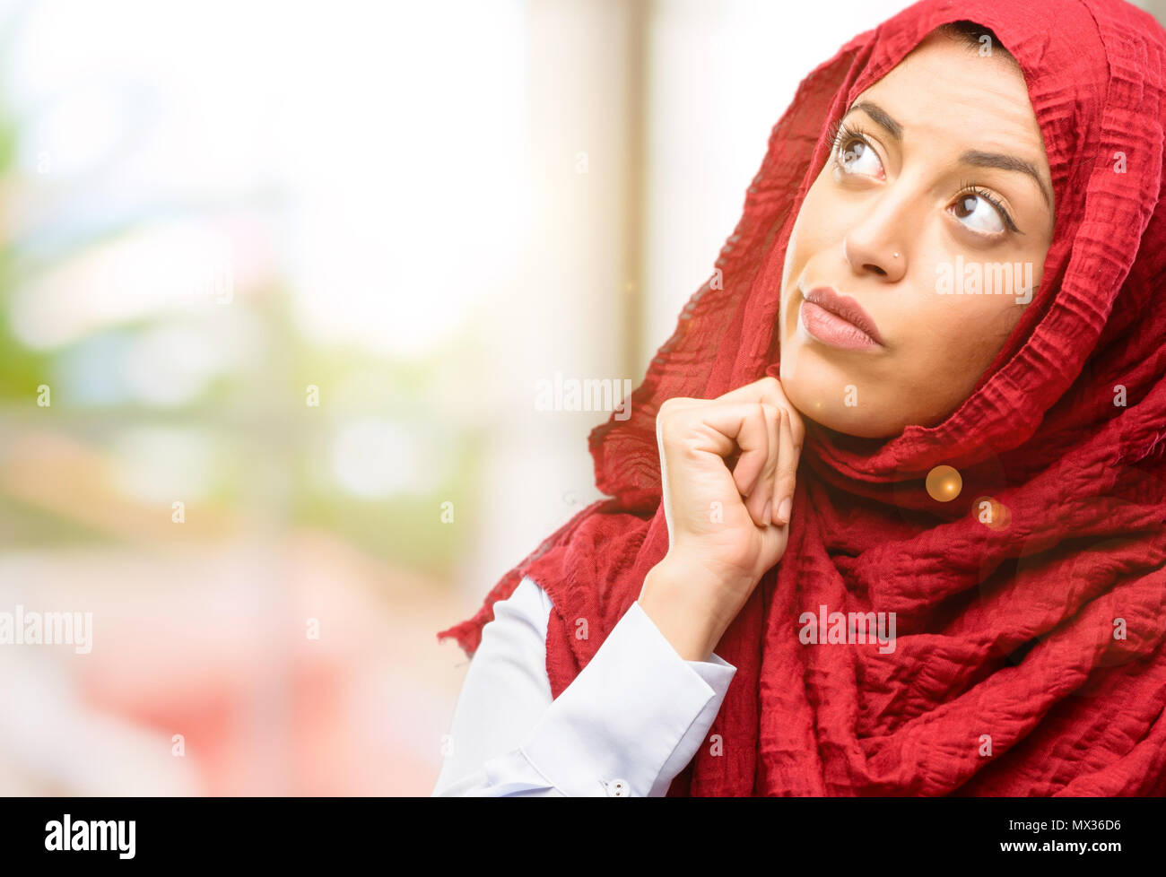Young arab woman wearing hijab thinking and looking up expressing doubt ...