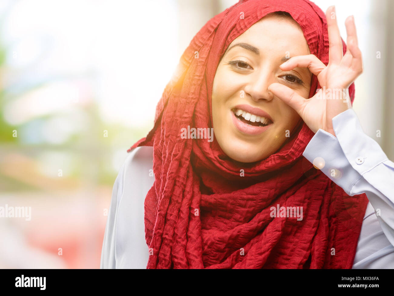 Young arab woman wearing hijab looking at camera through her fingers in ...