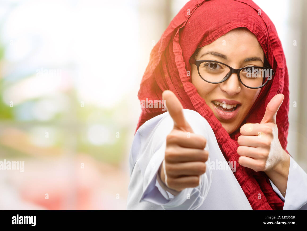 Young arab woman wearing hijab stand happy and positive with thumbs up ...