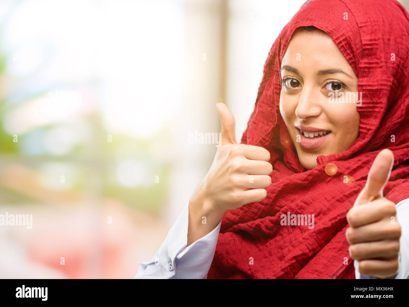 Young arab woman wearing hijab stand happy and positive with thumbs up ...