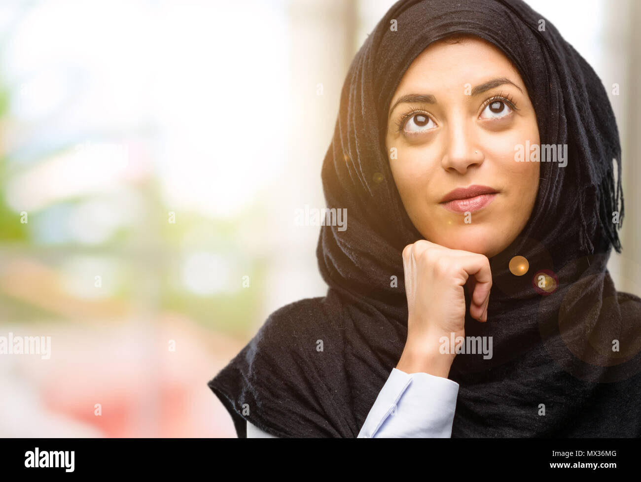 Young arab woman wearing hijab thinking and looking up expressing doubt ...