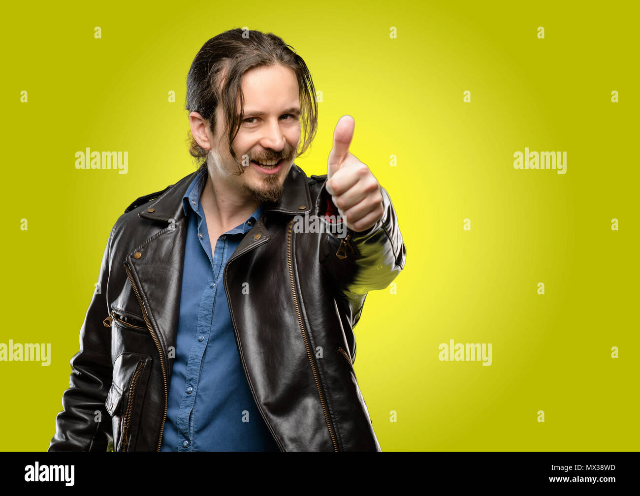 Handsome young man smiling broadly showing thumbs up gesture to camera ...