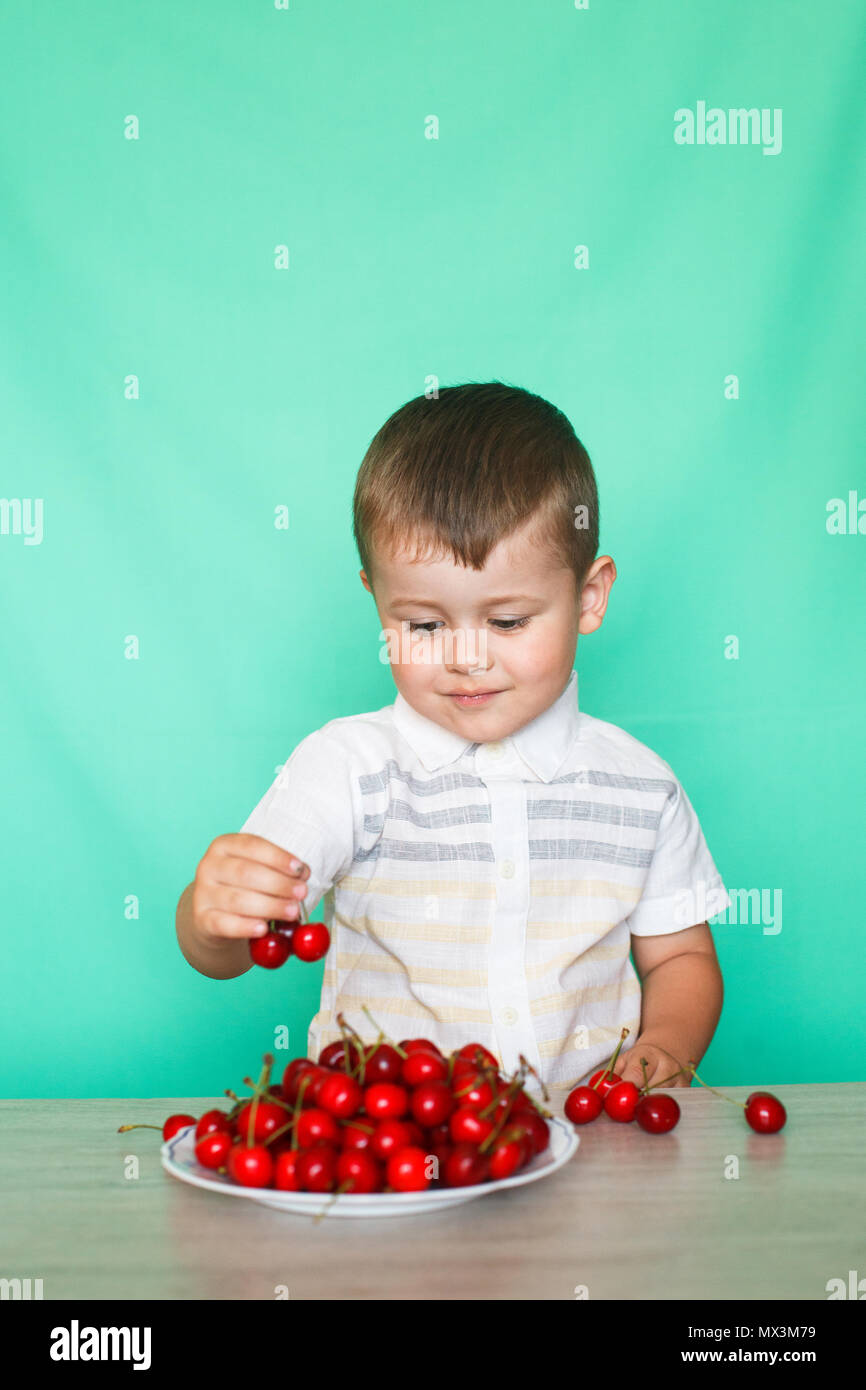 Cute boy boy eating ripe cherries Stock Photo - Alamy