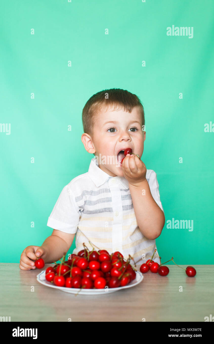 Cute boy boy eating ripe cherries Stock Photo - Alamy