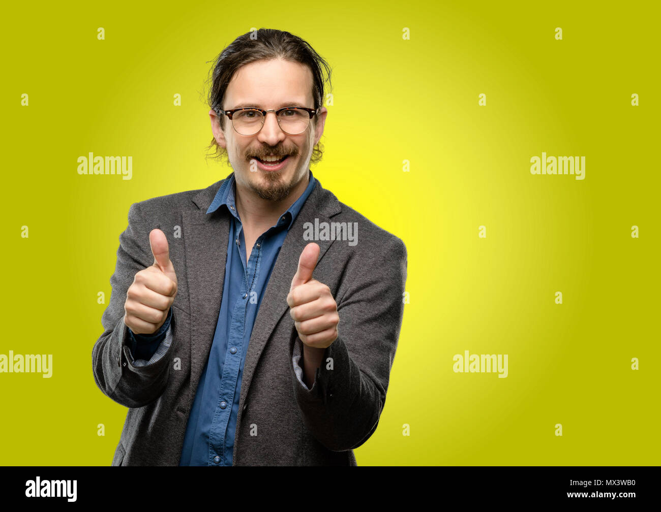 Handsome young man smiling broadly showing thumbs up gesture to camera ...