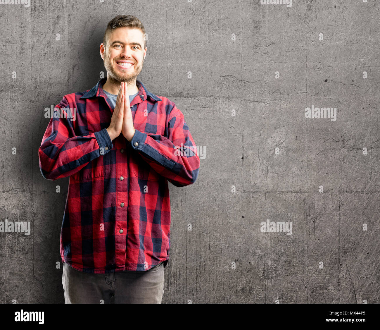 Young handsome man with hands together in praying gesture, expressing ...