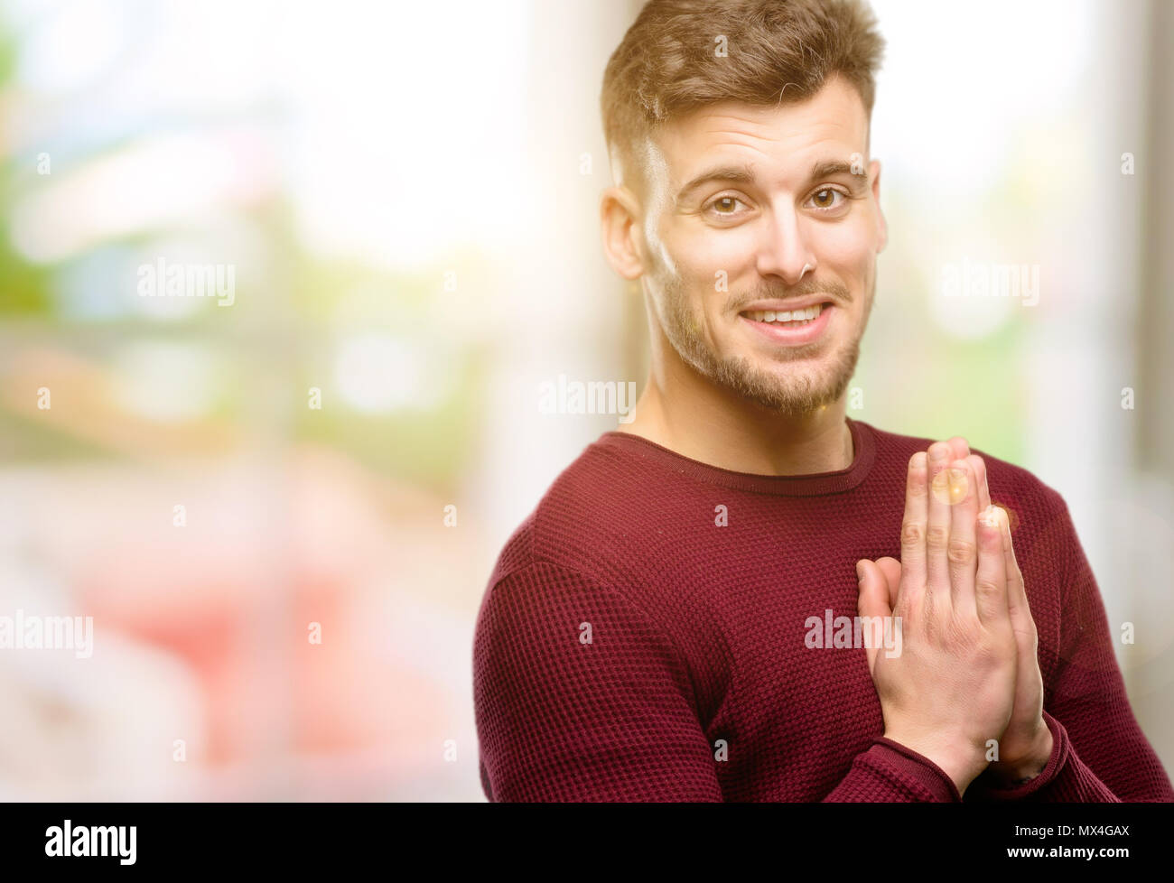 Handsome young man with hands together in praying gesture, expressing ...